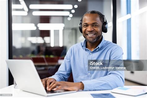 밝은 현대 사무실에서 노트북으로 작업하는 헤드폰을 착용하고 웃는 성숙한 아프리카 계 미국인 사업가 경영자에 대한 스톡 사진 및 기타 이미지 Istock