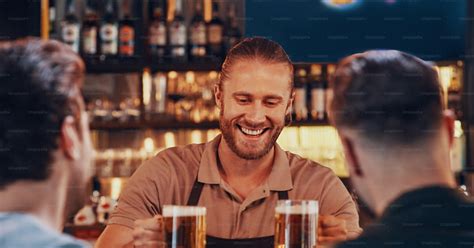 펍의 바 카운터에 서 있는 동안 젊은이들에게 맥주를 제공하는 쾌활한 바텐더 사진 Unsplash의 선술집 이미지