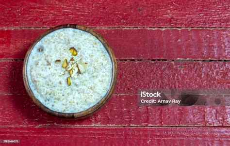 아몬드 캐슈 피스타치오로 장식된 금이 간 밀 Kheer 또는 Payesh의 평면도 복사 공간이 있는 빨간색 나무 배경에 고립된 나무 그릇 Ksheeram 우유 푸딩이라고도
