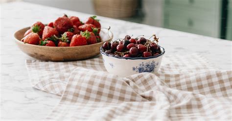 대리석 상판이 있는 주방 섬의 테이블 천에 체리와 딸기로 가득 찬 그릇 한 쌍 흐릿한 배경의 녹색 빈티지 가구 꽃으로 가득