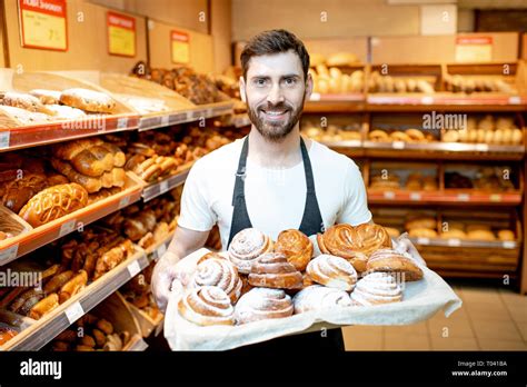 Portrait of a handsome baker in uniform standing with fresh pastries in ...