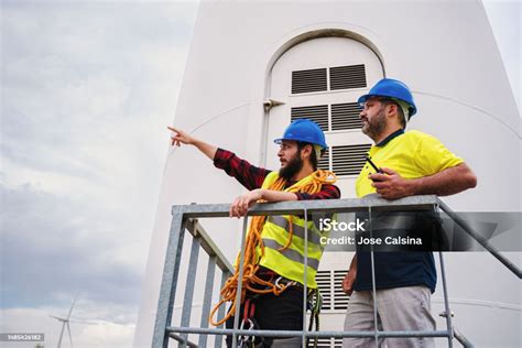 두 명의 풍차 엔지니어가 유지 보수를 해야 하는 터빈을 가리키고 있습니다 재생 에너지 기술자 전문가가 이야기를 나누고 함께 작업하고 발전기를 점검하여 전력을 점검합니다 2