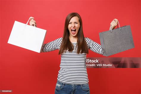 성 난 젊은 여자 비명 확산 손 밝은 빨간 벽 배경에 고립 쇼핑 후 구매와 패키지 가방을 들고 사람들이 진심으 감정 라이프 스타일 개념 복사 공간을 비웃는 다 갈색 머리에