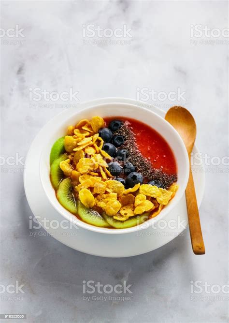 스무디 딸기 건강 한 아침 식사를 시리얼으로 그릇 과일 밀 밀기 울 콘플레이크 Chia 씨와 코코넛 칩은 갓 썬 백색 대리석 테이블에 나무 숟가락으로 제공 0명에 대한 스톡