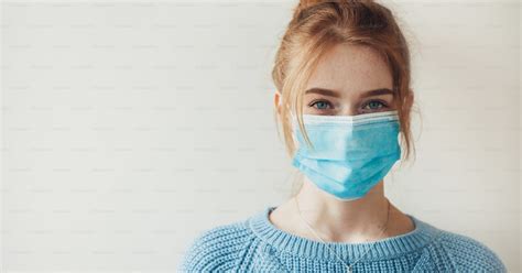 주근깨가 있는 빨간 머리 백인 여성은 의료용 마스크를 쓰고 여유 공간이 있는 흰색 스튜디오 벽에 카메라를 보고 있다 사진