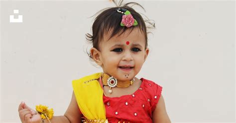 빨간색과 노란색 드레스를 입은 소녀가 흰색과 빨간색 꽃 직물에 앉아 사진 Unsplash의 무료 인도 이미지