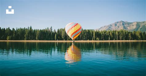 낮에는 푸른 하늘 아래 나무와 수역 근처의 노란색 빨간색 파란색 열기구 사진 Unsplash의 무료 산 이미지
