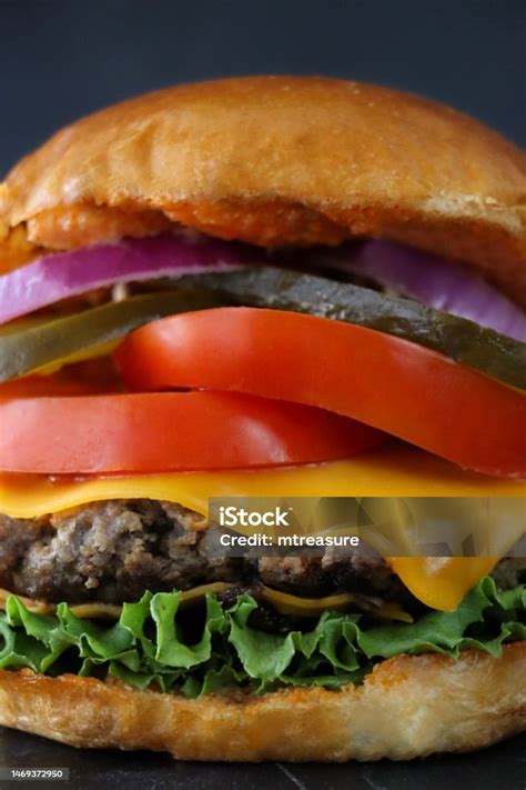 수제 치즈버거 햄버거 패티 녹는 가공 치즈 조각 양상추 잎 얇게 썬 토마토 피클과 적양파 조각 검은색 배경 전경에 초점 0명에
