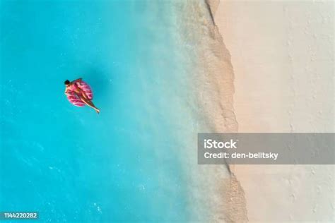 여름의 석양에 파도와 맑은 푸른 바다에서 도넛 수영 반지와 수영 하는 젊은 여자의 공중 보기 소녀 푸른 물 모래 해변과 열 대 공중 풍경입니다 평면도 여행 경관에 대한 스톡