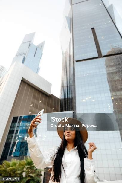 트렌디 한 외모로 웃는 여성 솔로 여행자가 휴대 전화에서 셀카를 만들고 카타르 도하를 배경으로 고층 빌딩을 만듭니다 인플루언서에 대한 스톡 사진 및 기타 이미지 Istock