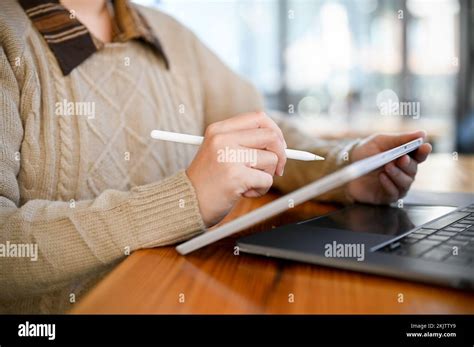 Side View Asian Female In Cozy Sweater Using Her Digital Tablet At Her Desk In Front Of The