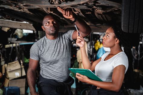 두 명의 정비사가 차고에서 자동차 아래 부품을 검사하고 체크리스트합니다 수리 자동차 서비스 개념 검사 보기에 대한 스톡 사진 및