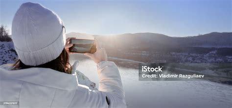 겨울 모험 여행에서 자연 사진 찍기 흰 재킷을 입은 소녀가 높은 둑에서 아름다운 강과 산의 사진을 찍습니다 뒷모습 흰 옷을 입은 사람이 즐겁게 사진을 찍고 있습니다 35