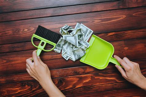 두 명의 여성 손이 붓을 들고 떠서 갈색 나무 테이블에서 달러 지폐를 꺼냅니다 평가 절하 감가 상각 인플레이션 및 채무 불이행의 개념은 돈이 가치를 잃을 때입니다 가계에