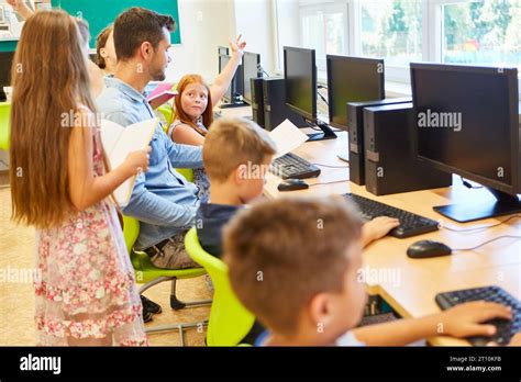 Male And Female Elementary Students Discussing With Teacher In Computer Class At School Stock