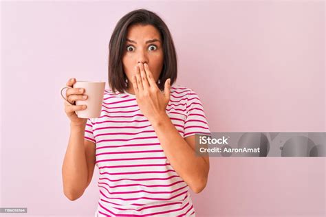 실수 공포의 표정 침묵 비밀 개념에 무서워 손으로 고립 된 분홍색 배경 커버 입 위에 서있는 커피 잔을 마시는 젊은 아름다운 여성 가리기에 대한 스톡 사진 및 기타 이미지