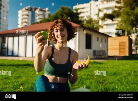 Young Redhead Sportive Woman Wearing Green Sports Bra And Blue Yoga Pants Showing Green Apple