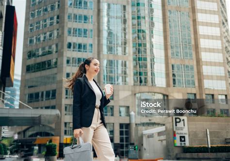 젊은 사업가는 현대적인 사무실 건물을 배경으로 커피 컵과 노트북 가방을 들고 도시를 걷고 있으며 바쁜 도시 생활을 즐기고 있습니다 20 29세에 대한 스톡 사진 및 기타