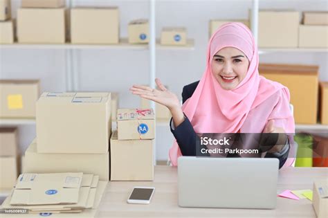 무슬림 정장을 입은 활동적인 아시아 여성이 앉아서 컴퓨터 모바일 스마트폰 온라인 소포 상자 배달을 하고 있다 스타트업 중소기업 프리랜서 일하는 소녀가 손에 무언가를 보여주고