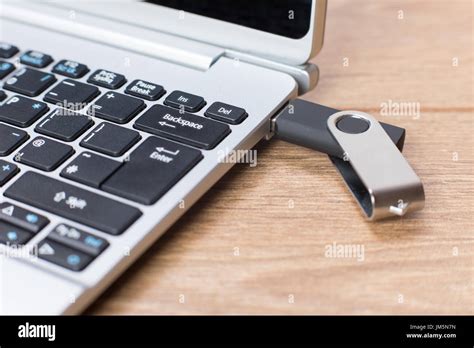 USB Memory Stick Or Flash Drive Attached To The Side Of A Laptop Computer On A Wooden Office