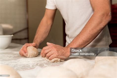 베이커리 공장의 젊은 남성 베이커는 조리대에서 밀가루로 반죽한 신선한 빵을 수동으로 반죽합니다 빵 공장에서 전통 수동 빵 준비의 개념 공장 산업 건물에 대한 스톡 사진 및