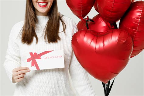 생일 휴가 파티를 축하하는 스웨터 빨간 모자 안경을 착용한 재미있는 젊은 여성의 자른 이미지는 흰색 배경 스튜디오에서 고립 된 헬륨 풍선을 부풀린 기프트 인증서 무리 심장