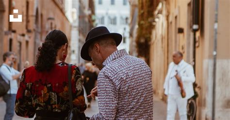 빨간색 주황색 회색 꽃무늬 드레스를 입은 여자 옆에 흰색과 회색 드레스 셔츠를 입은 남자가 집 밖에 서 있습니다 사진 Unsplash의 무료 음악 이미지