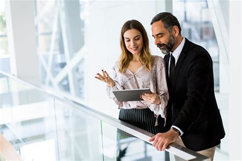 잘생긴 웃는 성숙한 사업가와 그의 귀여운 젊은 여성 동료와 디지털 태블릿에 사무실 2명에 대한 스톡 사진 및 기타 이미지 2