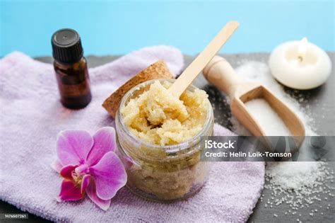 장식용 재료 숟가락과 아로마 오일에 설탕 파란색 배경에 에센셜 오일이 있는 유리 항아리에 수제 설탕 스크럽의 측면 보기 분홍색