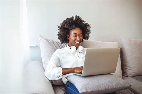 현대 헤드폰에 젊은 아프리카 계 미국인 여자 앉아 소파에 거실 이야기 에 노트북에 화상 통화 노트북에 대한 스톡 사진 및 기타 이미지 Istock