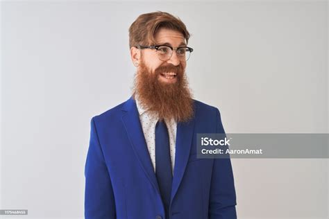 젊은 빨간 머리 아일랜드어 사업가 는 고립 된 흰색 배경 위에 양복과 안경을 입고 얼굴에 미소와 함께 옆으로 찾고 자연스러운 표정 자신감 있게 웃고 있습니다 감정에 대한