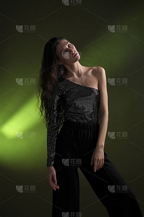 一个美丽的年轻高个女孩与黑色长发摆姿势在绿色背景上一件闪亮的衬衫和黑色的裤裙Buty和时尚摄影