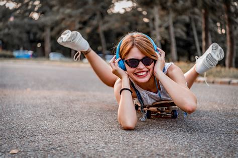 공원에서 사랑스러운 화창한 날에 스케이트 보드를 가진 아름다운 젊은 여성 헤드폰에 음악을 듣고 거리에 대한 스톡 사진 및 기타 이미지 Istock