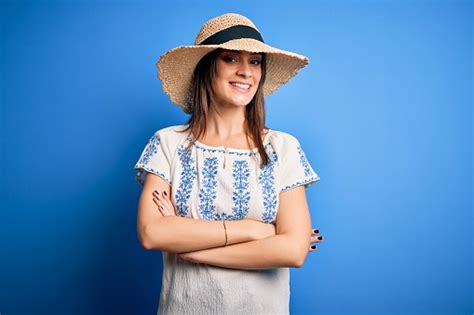 젊은 아름 다운 갈색 머리 여자 캐주얼 티셔츠와 여름 모자를 입고 푸른 배경 행복 한 얼굴 카메라를 보고 교차 팔 미소 긍정적 인 사람 T 셔츠에 대한 스톡 사진 및 기타