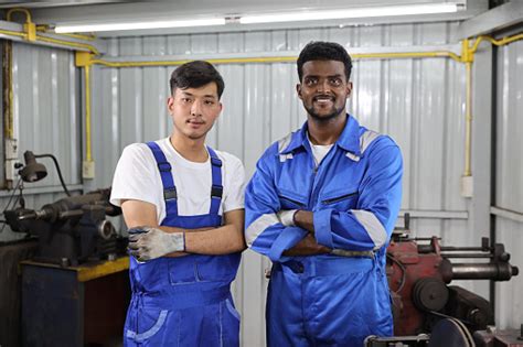 다민족 기술자 정비공은 금속 선반 기계에서 작업하는 동안 차고에서 자동차 디스크 브레이크 연마를 작동하면서 자신감을 가지고 팔짱을 끼었습니다 유지 보수 자동차 및 검사 차량