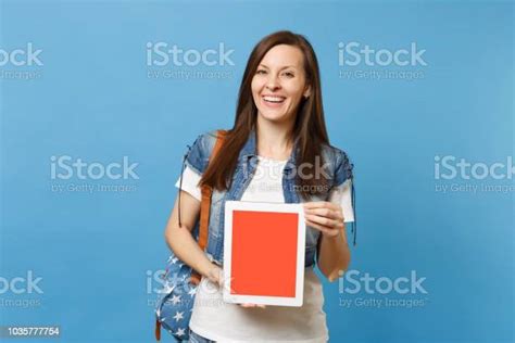 젊은 웃는 여자 학생 가방 들고 빈 검은색 빈 화면으로 태블릿 Pc 컴퓨터와 데님 옷에서 파란 배경에 고립 대학에서 교육입니다 광고에 대 한 공간을 복사 합니다 20 29