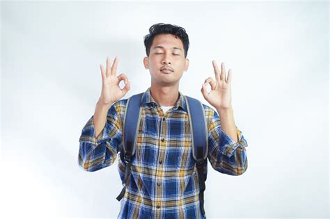 쾌활한 젊은 아시아 학생 남자가 흰색 배경에 고립 된 괜찮은 제스처를 보여주는 배낭을 가진 캐주얼 한 옷을 입고 있습니다 고등학교 대학 대학 개념 25 29세에 대한 스톡