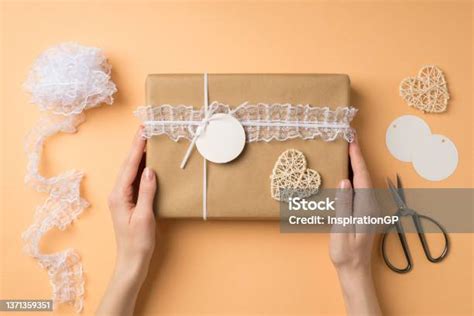 레이스 리본 트림과 카피 스페이스와 고립 된 베이지 색 배경에 레이스 등나무 하트의 태그 가위 스풀과 크래프트 종이 선물 상자를 들고 세인트 발렌타인 데이 장식 손의 1