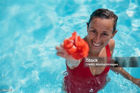 빨간 수영복을 입은 여자가 꽃을 들고 수영장 폭포 옆에서 휴식을 취하고 있습니다 30 39세에 대한 스톡 사진 및 기타 이미지