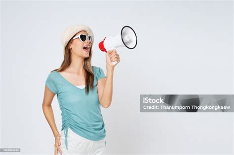 태양 모자를 쓰고 선글라스를 끼고 하얀 배경에 고립된 확성기를 들고 있는 젊은 여성 라이프 스타일 여름과 컨셉을 발표합니다