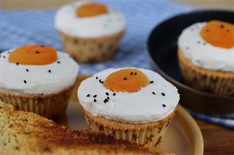 홈메이드 튀긴 달걀 바닐라 컵케이크의 클로즈업 이미지 흰색 파이프 착빙 프로스팅과 말린 살구를 종이 케이크 케이스에 얹고 구운 통밀 빵 삼각형 파란색 깅엄 식탁보 전경에