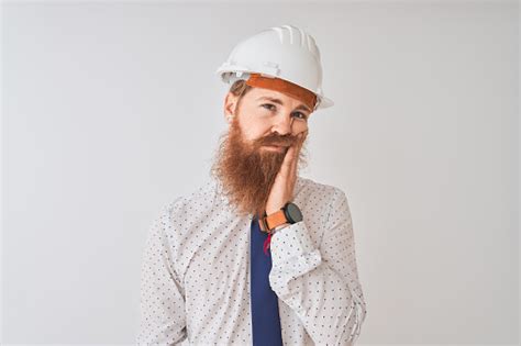 고립 된 흰색 배경 위에 보안 헬멧을 쓰고 있는 젊은 빨간 머리 아일랜드 건축가 남자는 피곤하고 교차 된 팔로 우울증 문제로