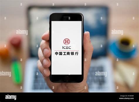 a man looks at his iphone which displays the icbc logo while sat at