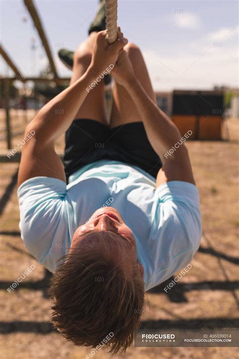Caucasian Male Fitness Coach At A Boot Camp On A Sunny Day Hanging Upside Down Holding A Rope