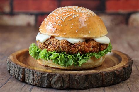 미식가가있는 미식가 나무 접시에 수제 치킨 버거 참깨를 곁들인 빵 만두 녹은 치즈와 양상추 벽돌 벽 배경 전경에 초점을 맞춘 미식가 펍 나무 테이블의 클로즈업 이미지 0명에