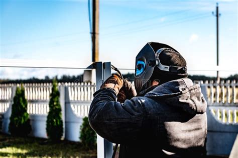 A Welder Wearing A Safety Helmet And Gloves Is Welding A Metal Fence