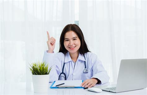 아시아 의사 젊은 아름다운 여자 노트북 컴퓨터와 그녀의 쓰기 뭔가 클립 보드 백서와 병원 데스크 사무실에서 손가락을 작성 하 여 웃고 의료 의료 개념 건강관리와 의술에 대한