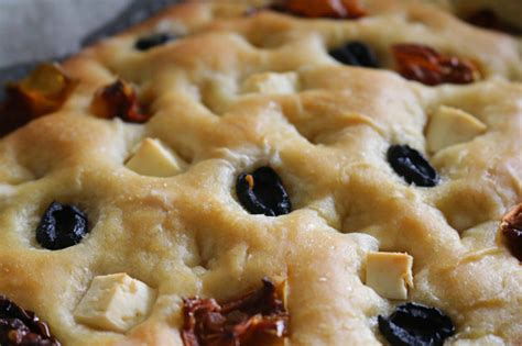 기름을 자은 종이 양피지 녹색 올리브 햇볕에 말린 토마토와 페타 치즈가 늘어선 베이킹 트레이에 집에서 만든 이탈리아 포카치아 빵 덩어리의 이미지 전경에 초점을 맞추고 0명에