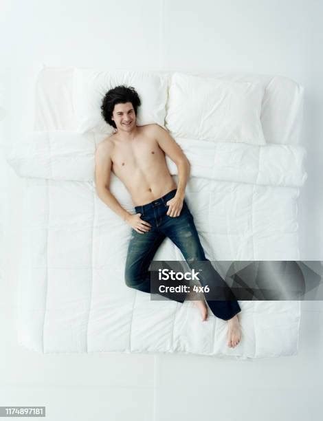 전체 길이 한 사람 한 사람 직접 위의 2029 세 잘 생긴 사람 긴 머리 백인 남성 청바지를 입고 침실에서 흰색 배경 앞에 누워 멋진 태도 유혹 20 24세에 대한 스톡