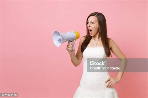 서 고 핑크 파스텔 배경에 고립 된 확성기에 우아한 하얀 웨딩 드레스에 충격된 신부 여자의 초상화 웨딩 컨셉의 조직입니다 광고에 대 한 공간을 복사 합니다 갈색 머리에 대한